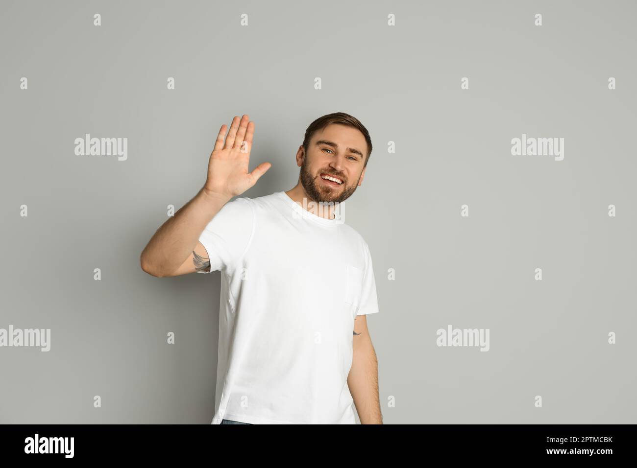 Happy young man waving to say hello on light grey background Stock ...