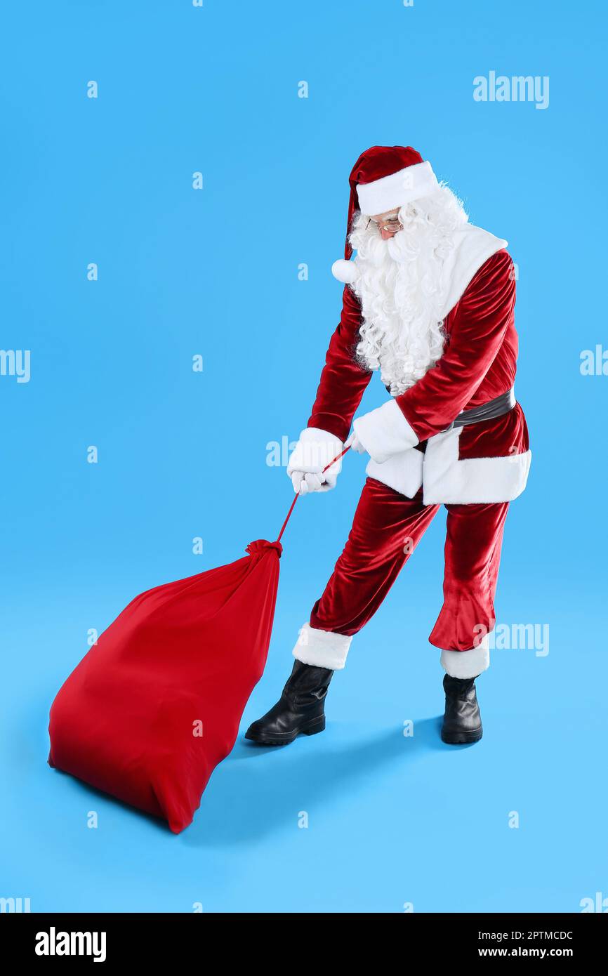 Full length portrait of Santa Claus pulling sack on light blue ...