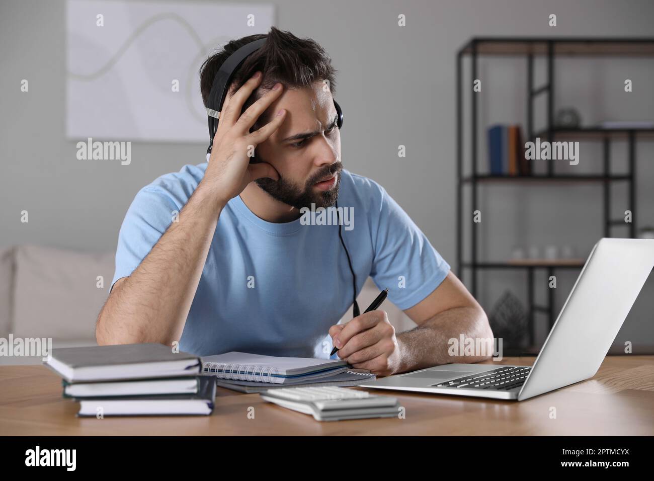 Confused young man watching webinar at table in room Stock Photo - Alamy