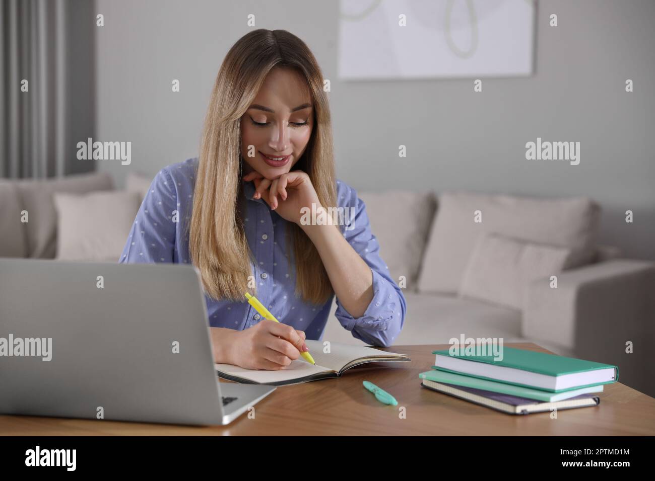 Young woman writing down notes during webinar at table in room Stock ...