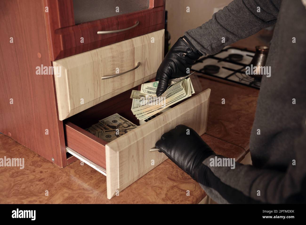 Robber in black outfit and gloves see in opened shelf in kitchen. The ...