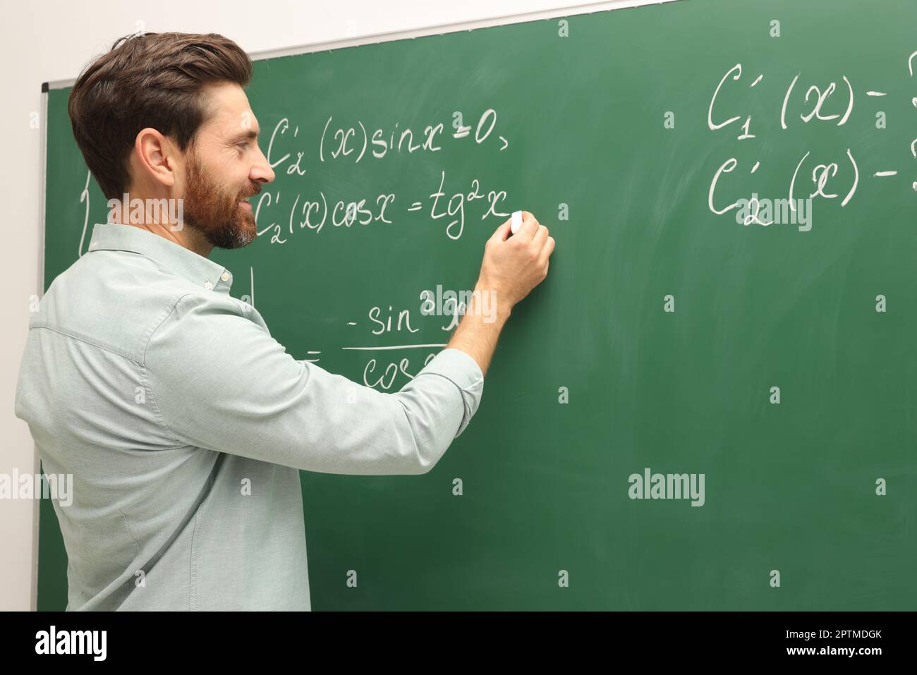 Happy teacher explaining mathematics at chalkboard in classroom Stock ...