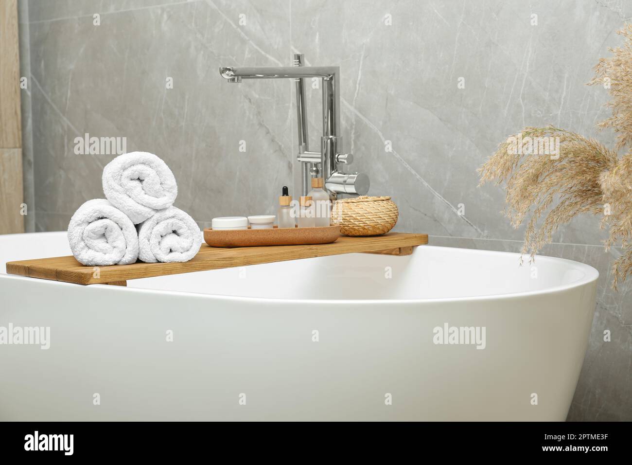 Rolled bath towels and personal care products on tub tray in bathroom ...