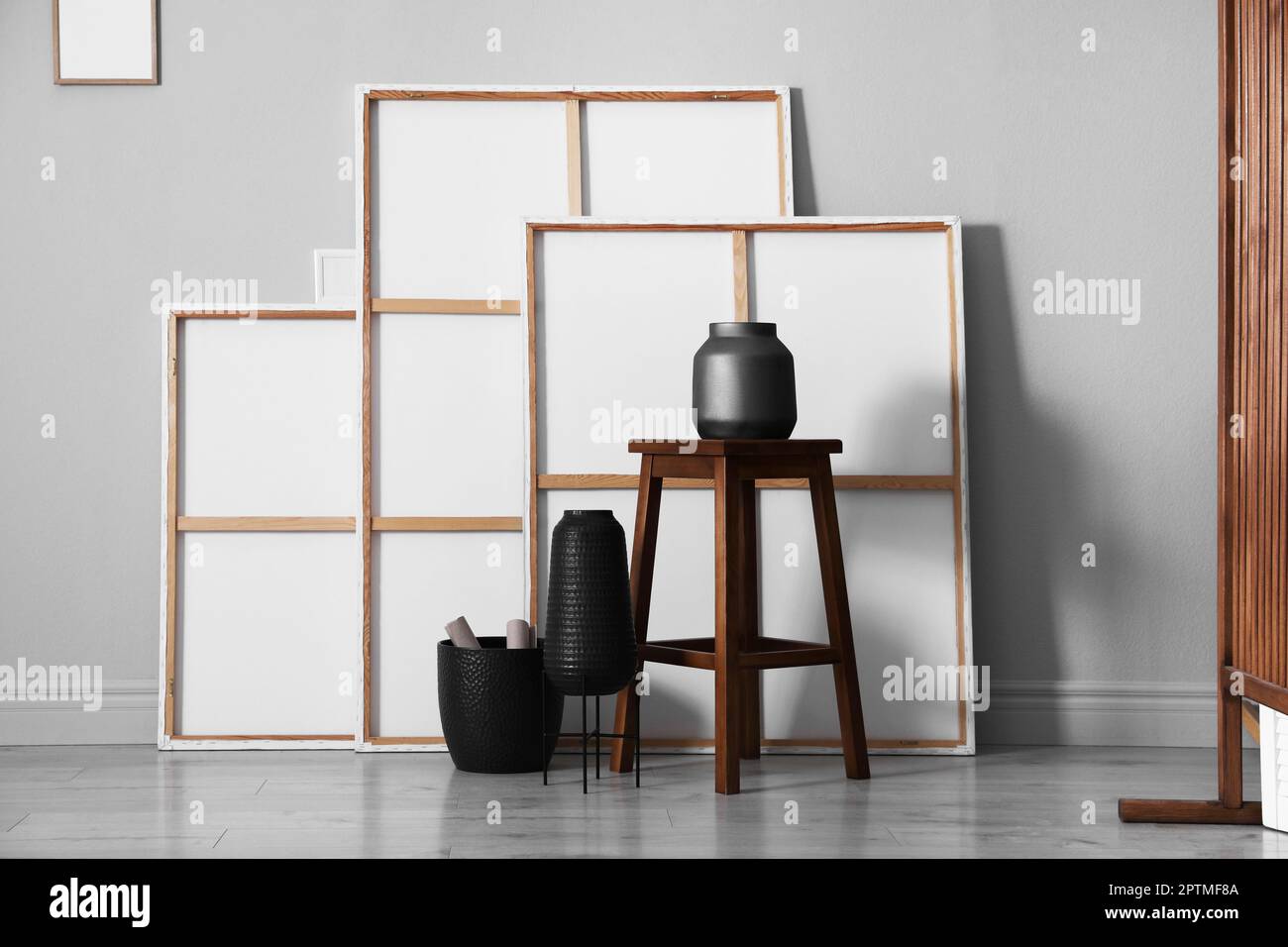 Many paintings, wooden stool and vases near grey wall in artist's ...