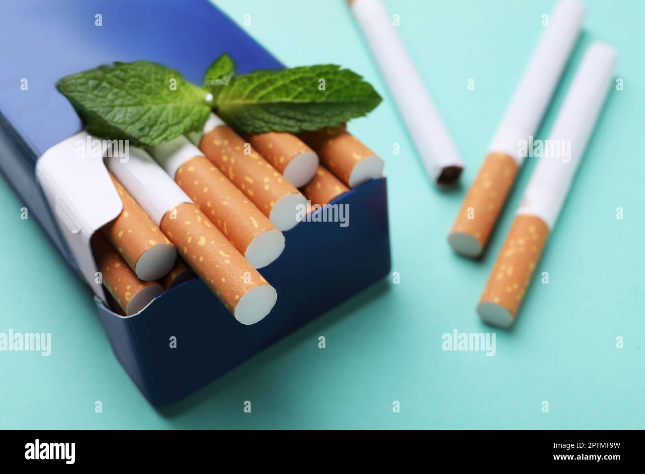 Pack of menthol cigarettes and mint on turquoise background, closeup ...
