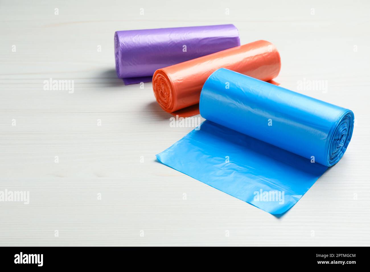 Rolls of different color garbage bags on white wooden table. Space for ...