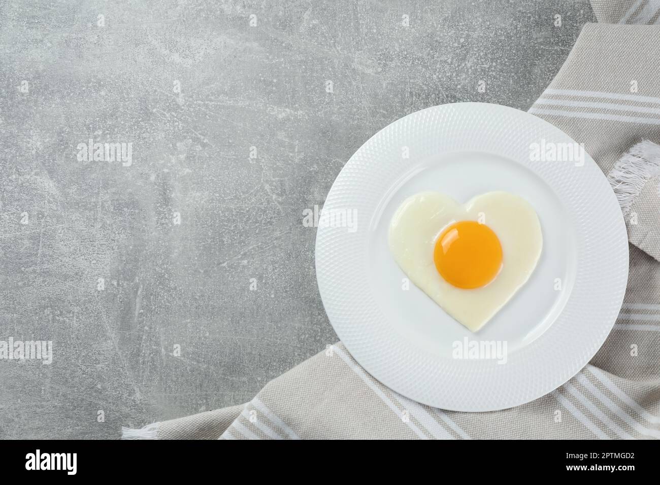 Romantic breakfast with heart shaped fried egg on light grey table, top view. Space for text ...