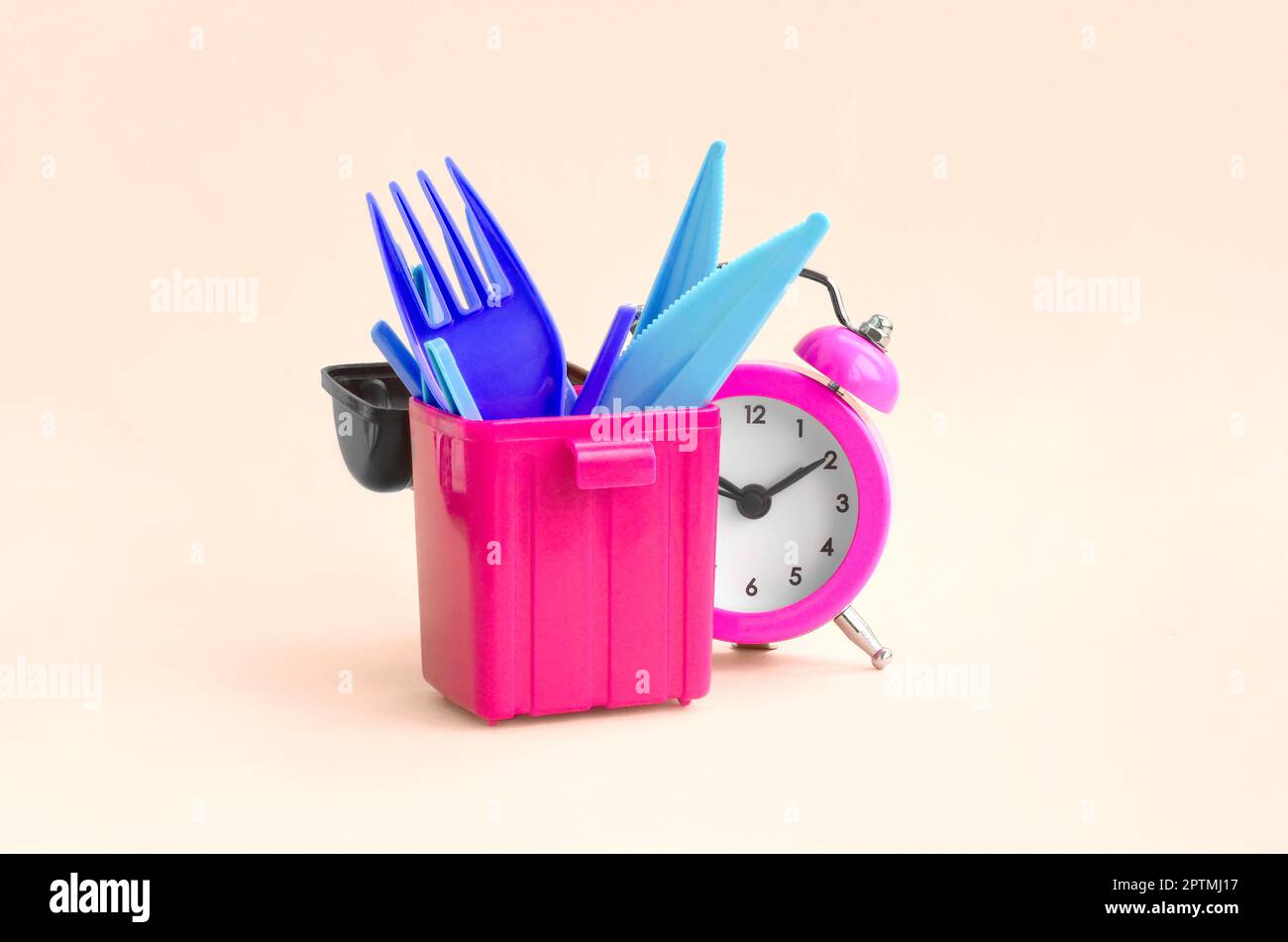 Alarm clock and plastic cutlery in trash bin on peach background. Time ...