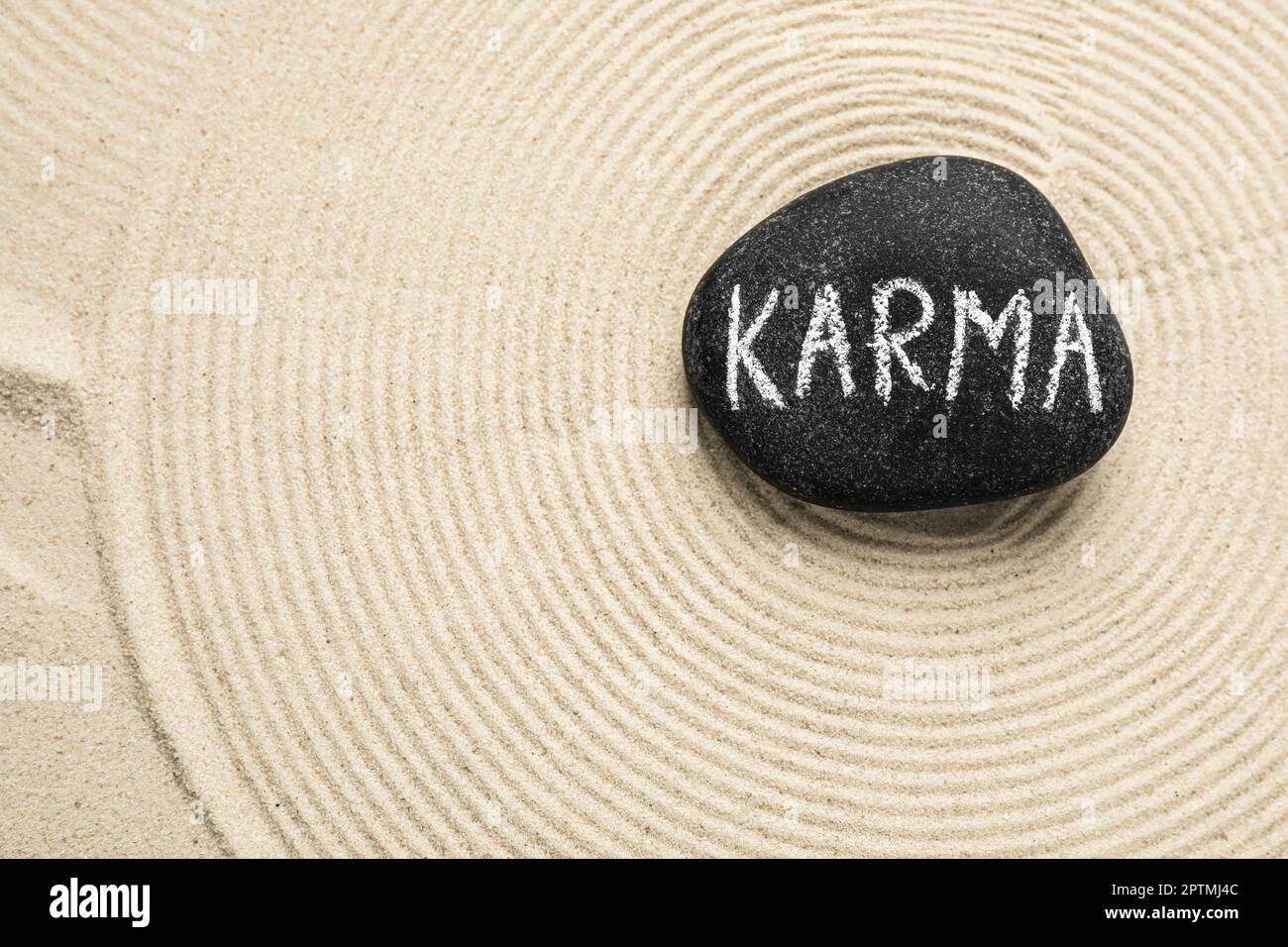 Stone with word Karma and circles on sand, top view. Space for text ...