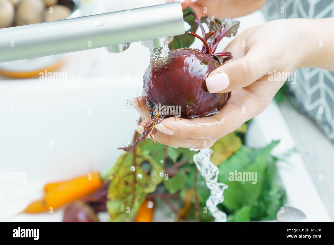 Female manicured hands washing fresh beet under tap water jet in ...