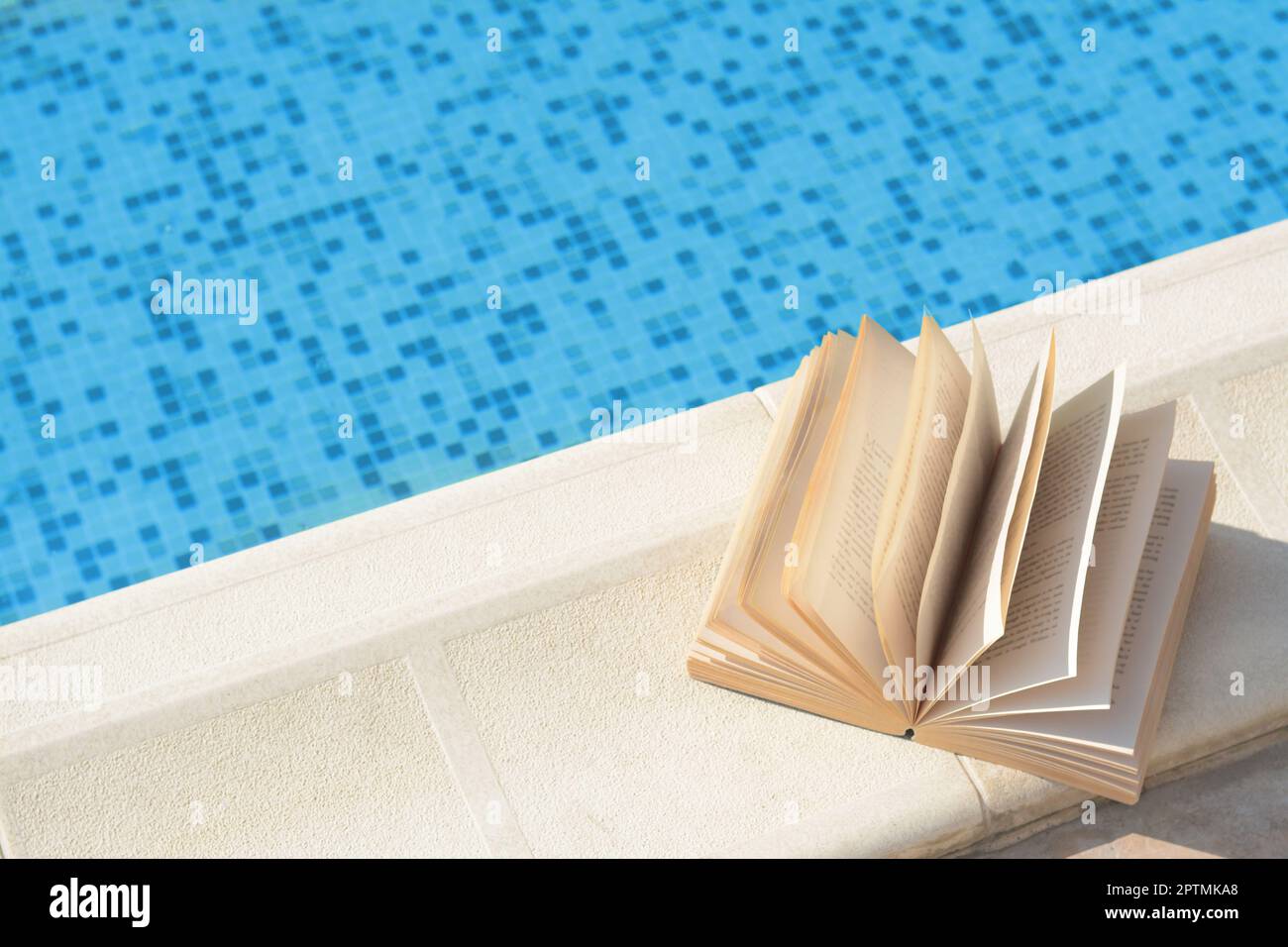 Open book on swimming pool edge during sunny day, above view. Space for ...