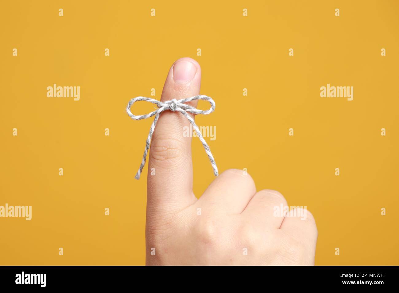 Man showing index finger with tied bow as reminder on orange background ...