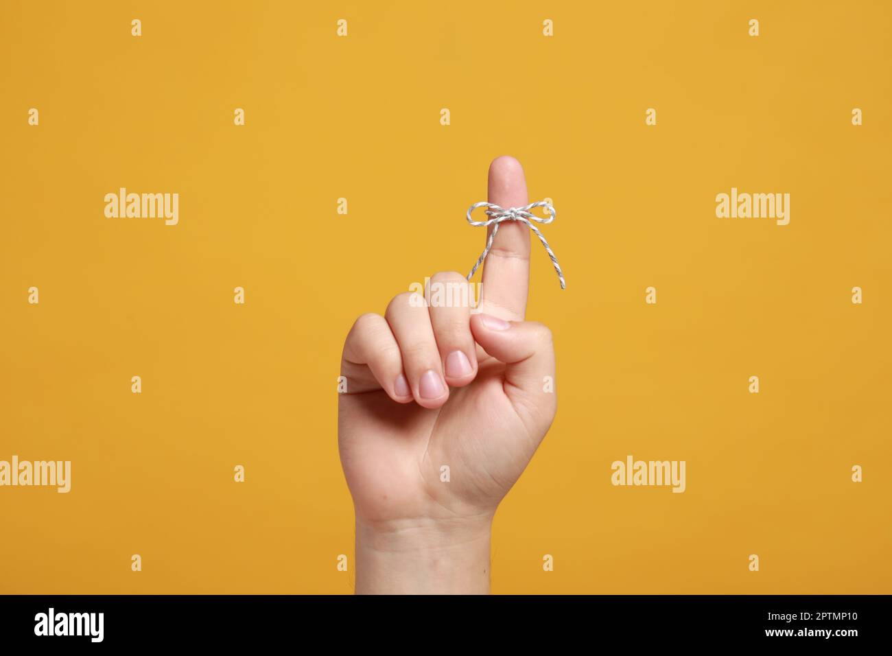Man showing index finger with tied bow as reminder on orange background ...