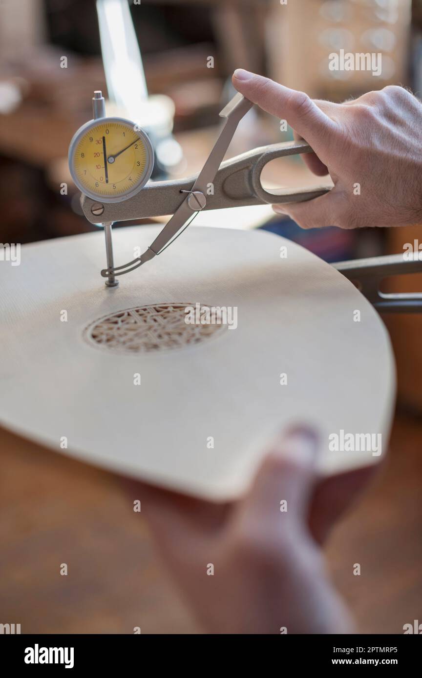 Craftsman measuring thickness of wood while manufacturing lute at ...