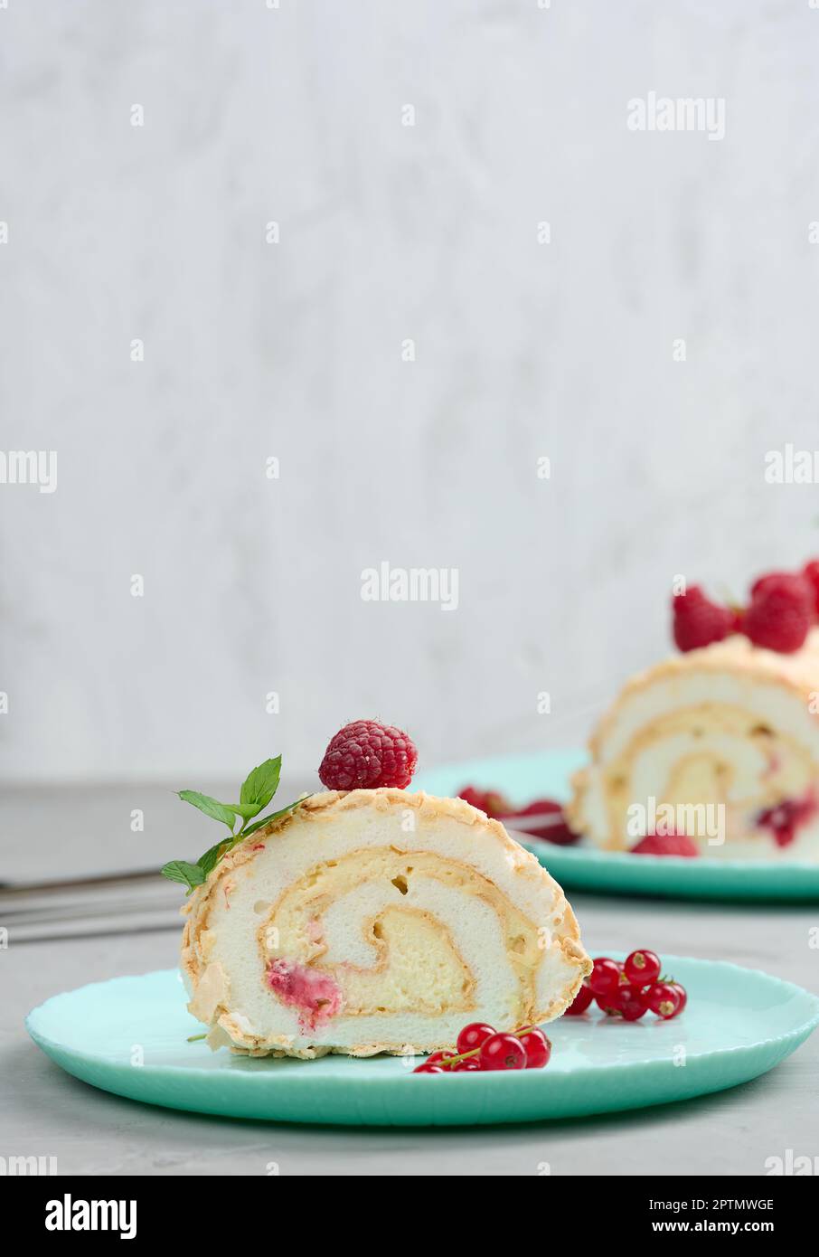 Baked meringue roll with red berries on a round plate, white background ...