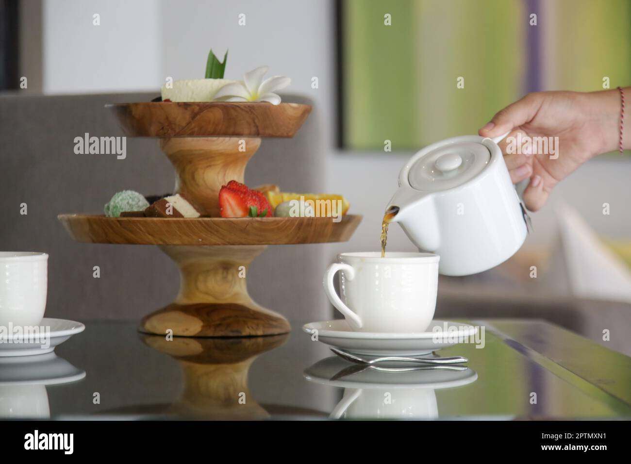 Woman hand holding a teapot and pouring tea in a white ceramic cup ...