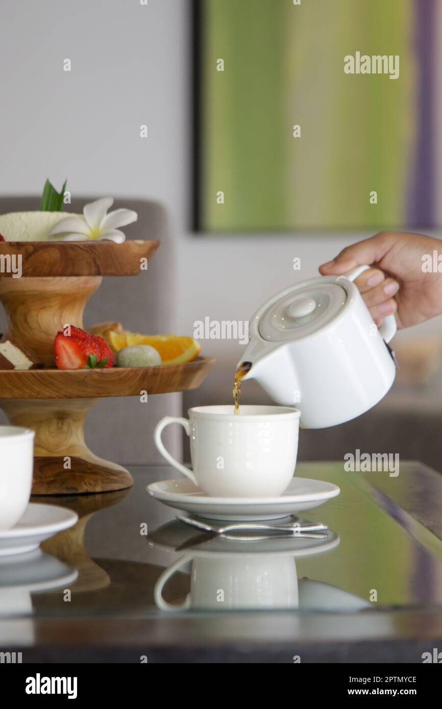 Woman hand holding a teapot and pouring tea in a white ceramic cup ...