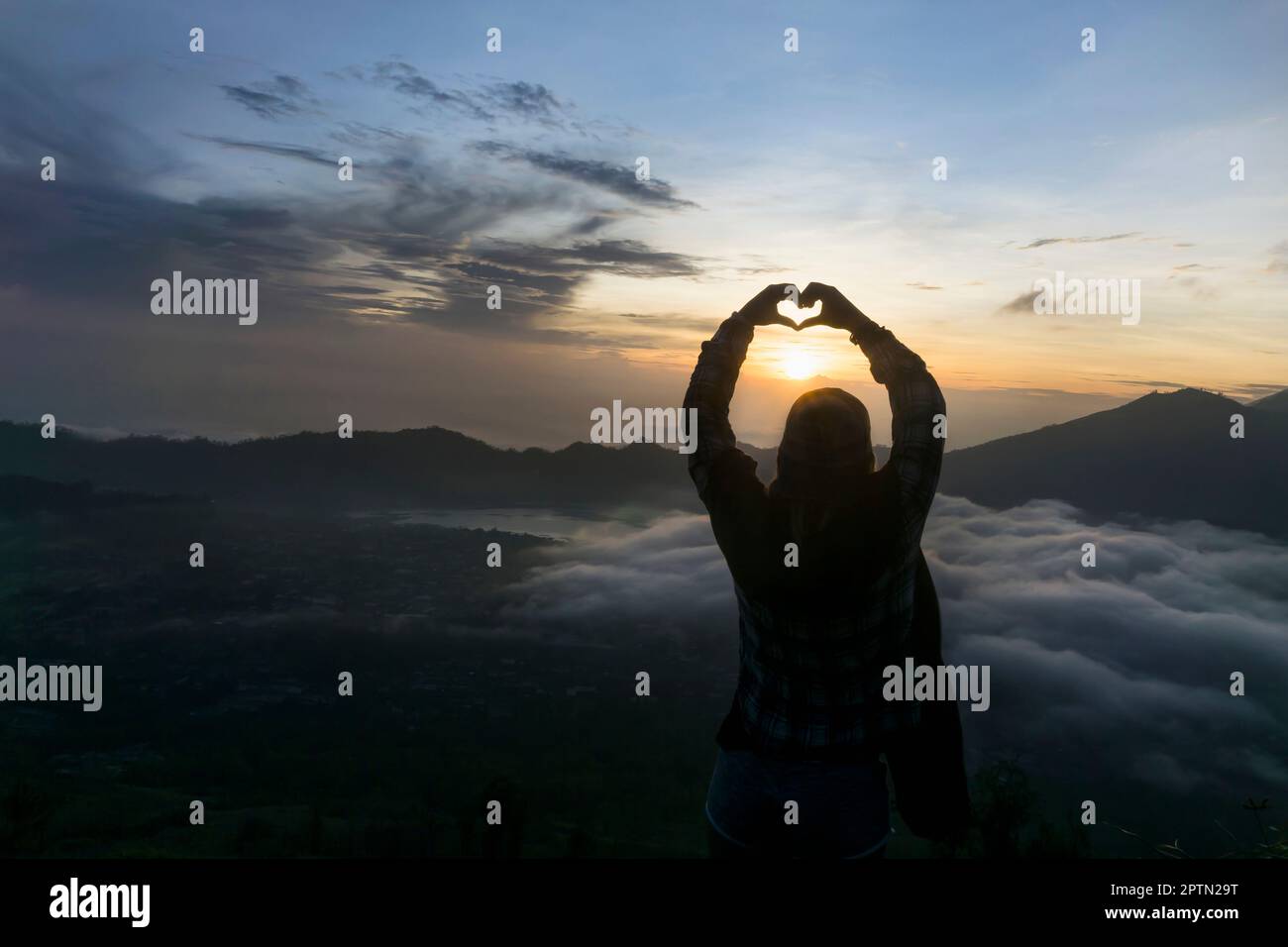 Silhouette of a young woman fingers forming a heart at dawn, Uluwatu ...