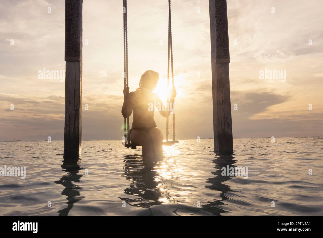 Woman sitting on rope swing at beach against sunset, Gili Trawangan ...