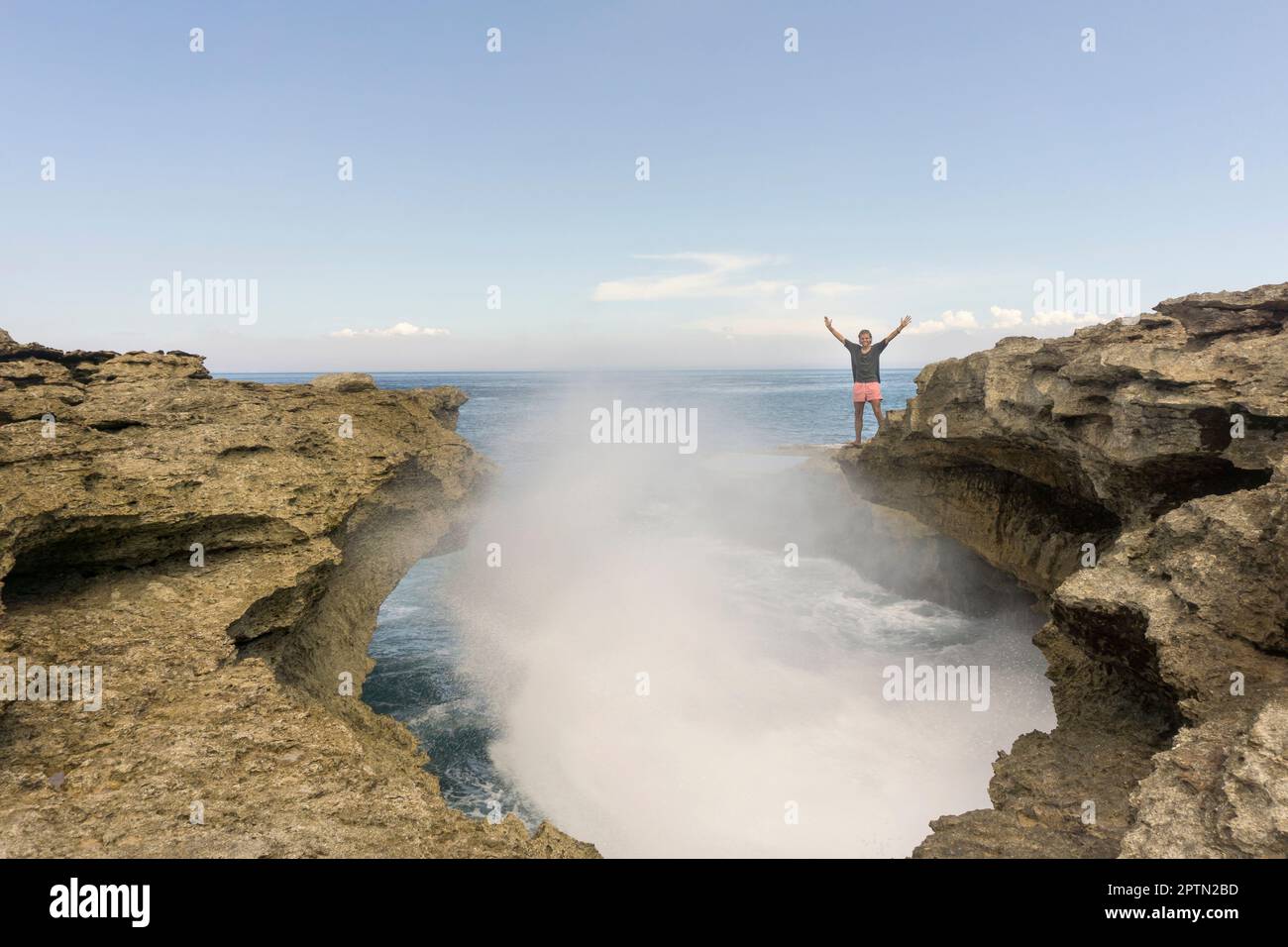 Young man standing on rock formation by splashed sea waves, Nusa ...