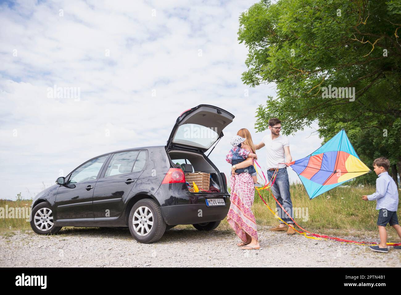 Family with kite unloading the car on meadow in the countryside ...