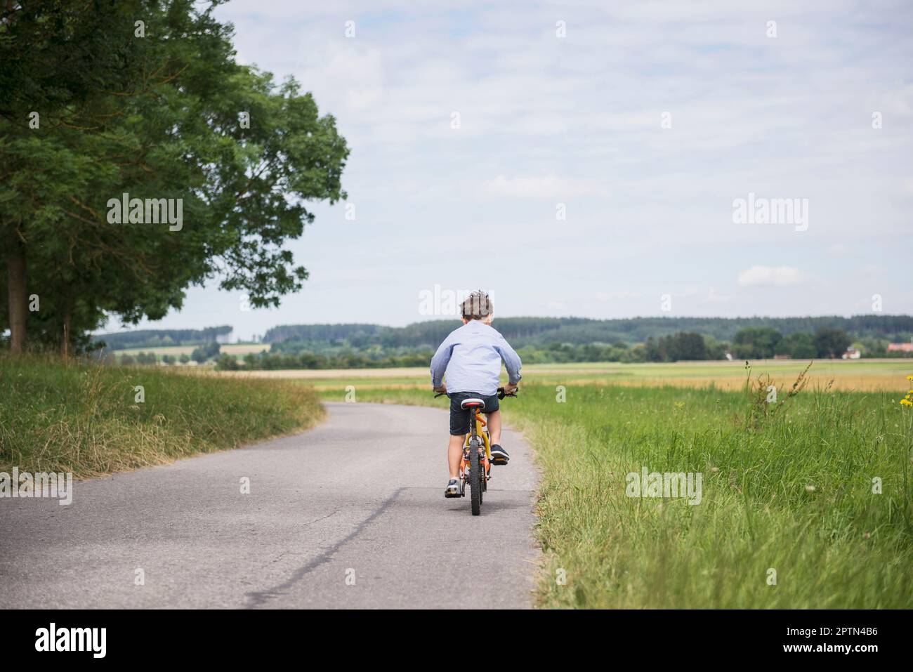 Rear view of a child riding bicycle on road in the countryside, Bavaria ...