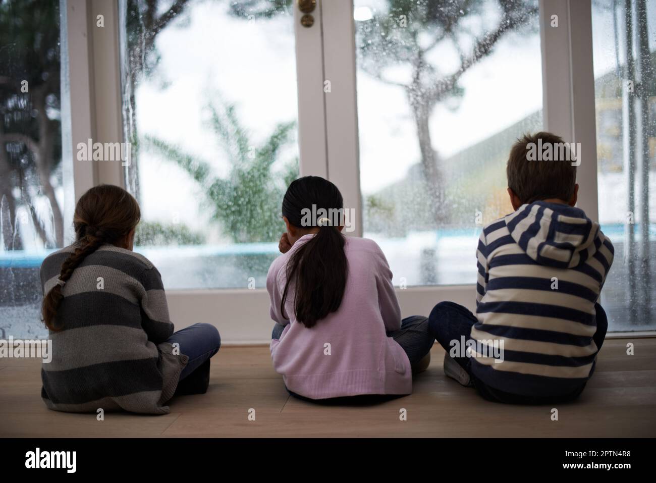 Rainy days with nothing to do...Rearview shot of three children looking ...