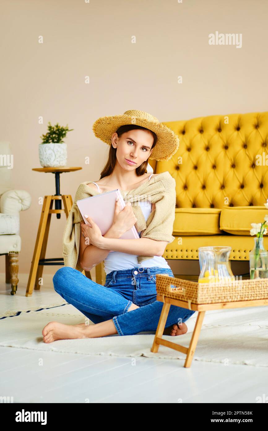 Barefoot girl holds the book sitting on the floor in apartment in ...