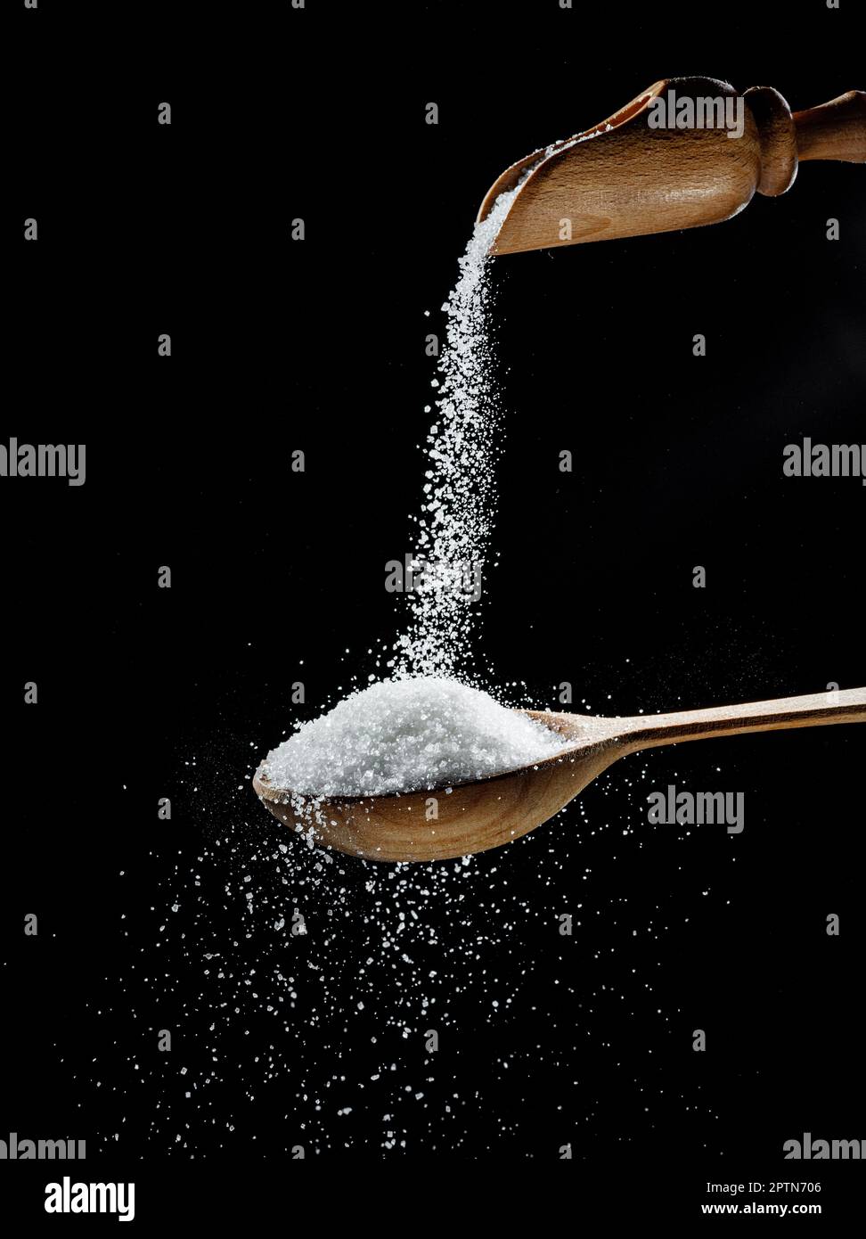 White refined sugar crystals falling down into the wooden spoon at ...