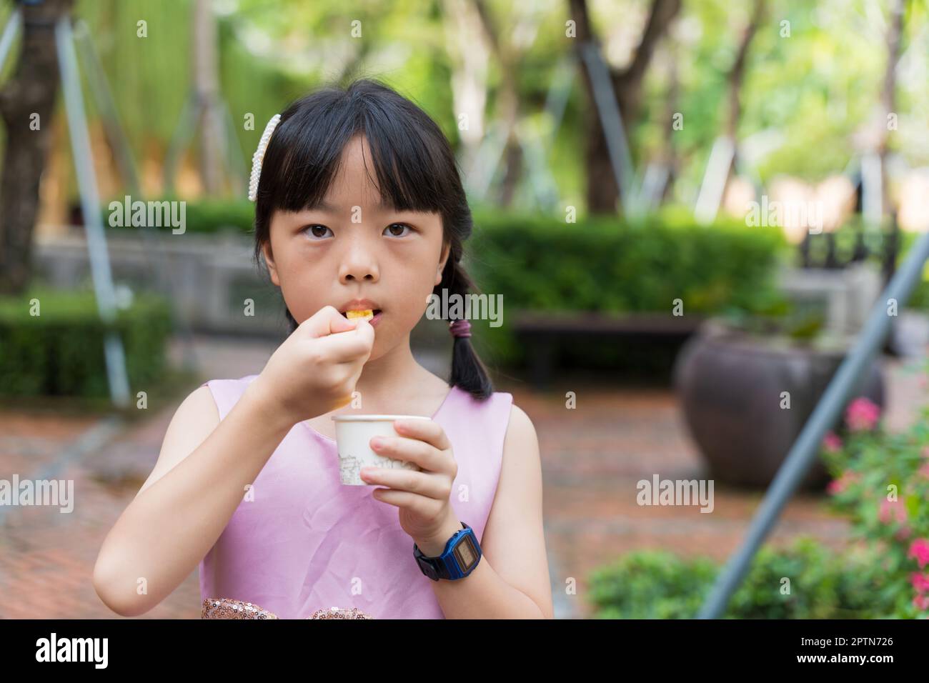 Portrait of a cute girl eating an ice cream cup in the park outdoors ...
