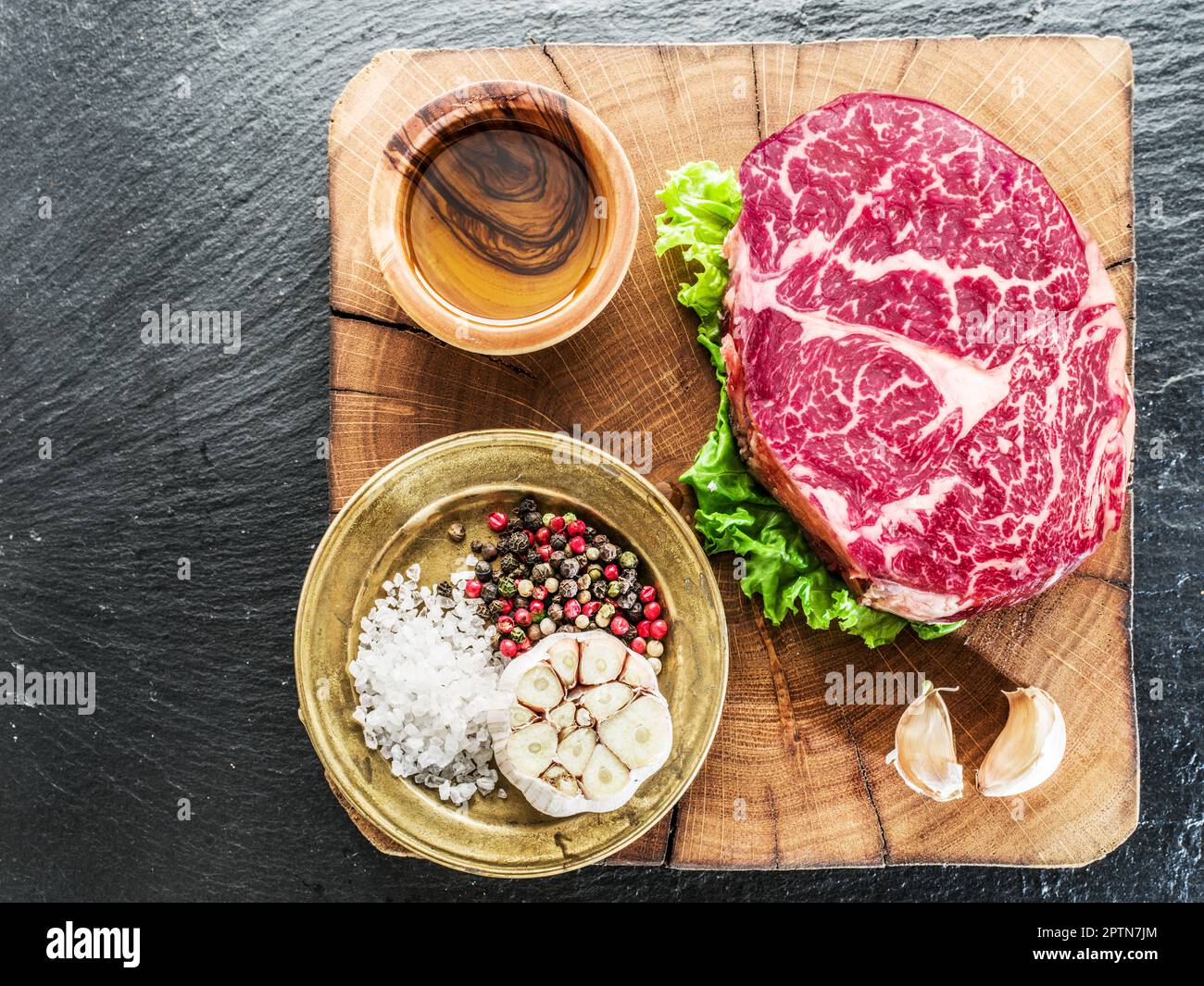 Raw ribeye steak with seasonings on wooden serving plate over gray ...