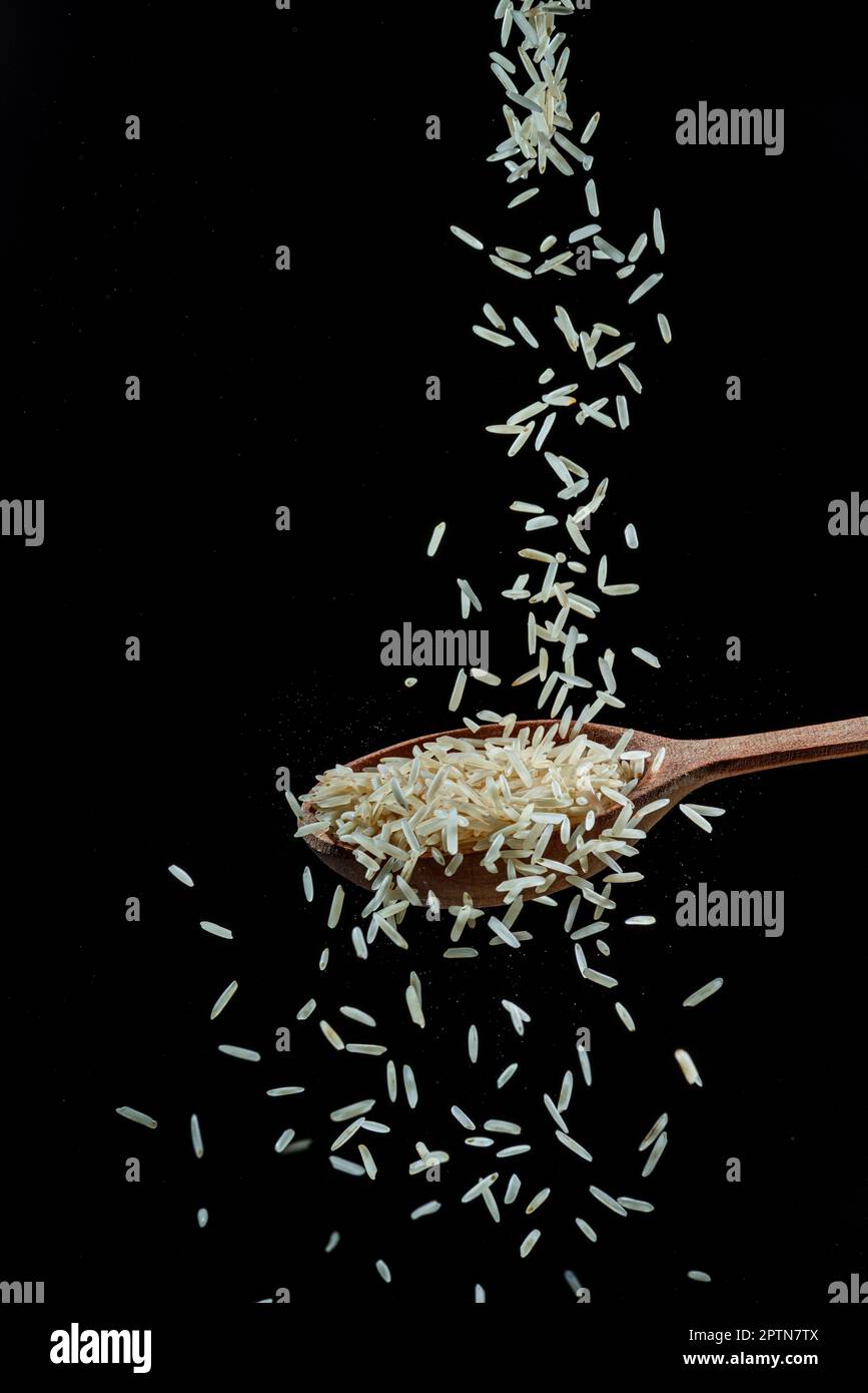 White rice grains falling down into the spoon at black background ...