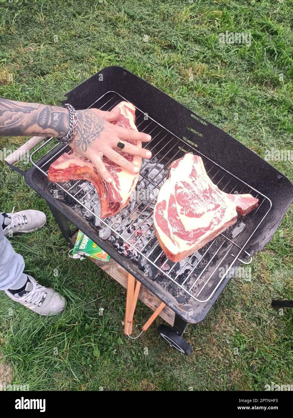 tatooed caucasian man hand Raw beef steak falls on grill with burning ...