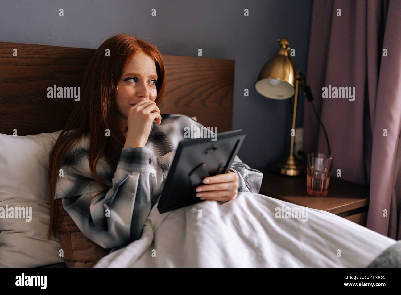 Closeup of grief-stricken young woman lying on bed under blanket ...