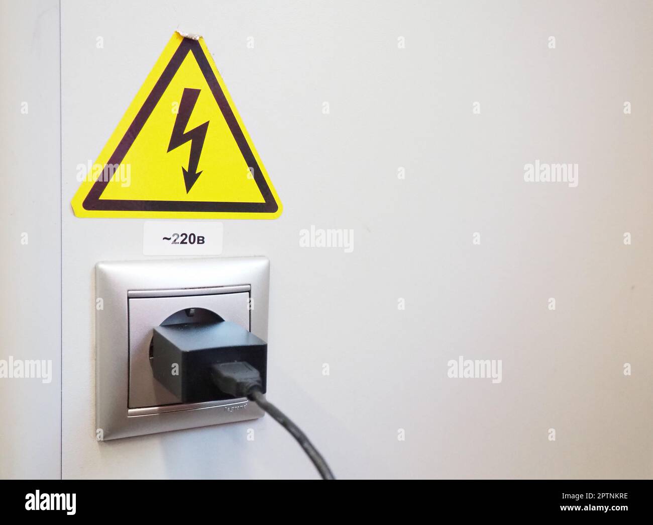 High-voltage sign on the white wall. A plug with a cable is stuck in an ...