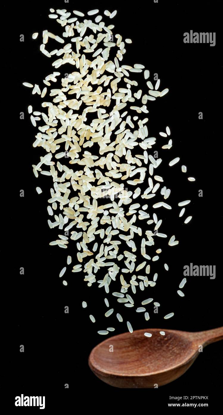 White rice grains falling down into the spoon at black background ...