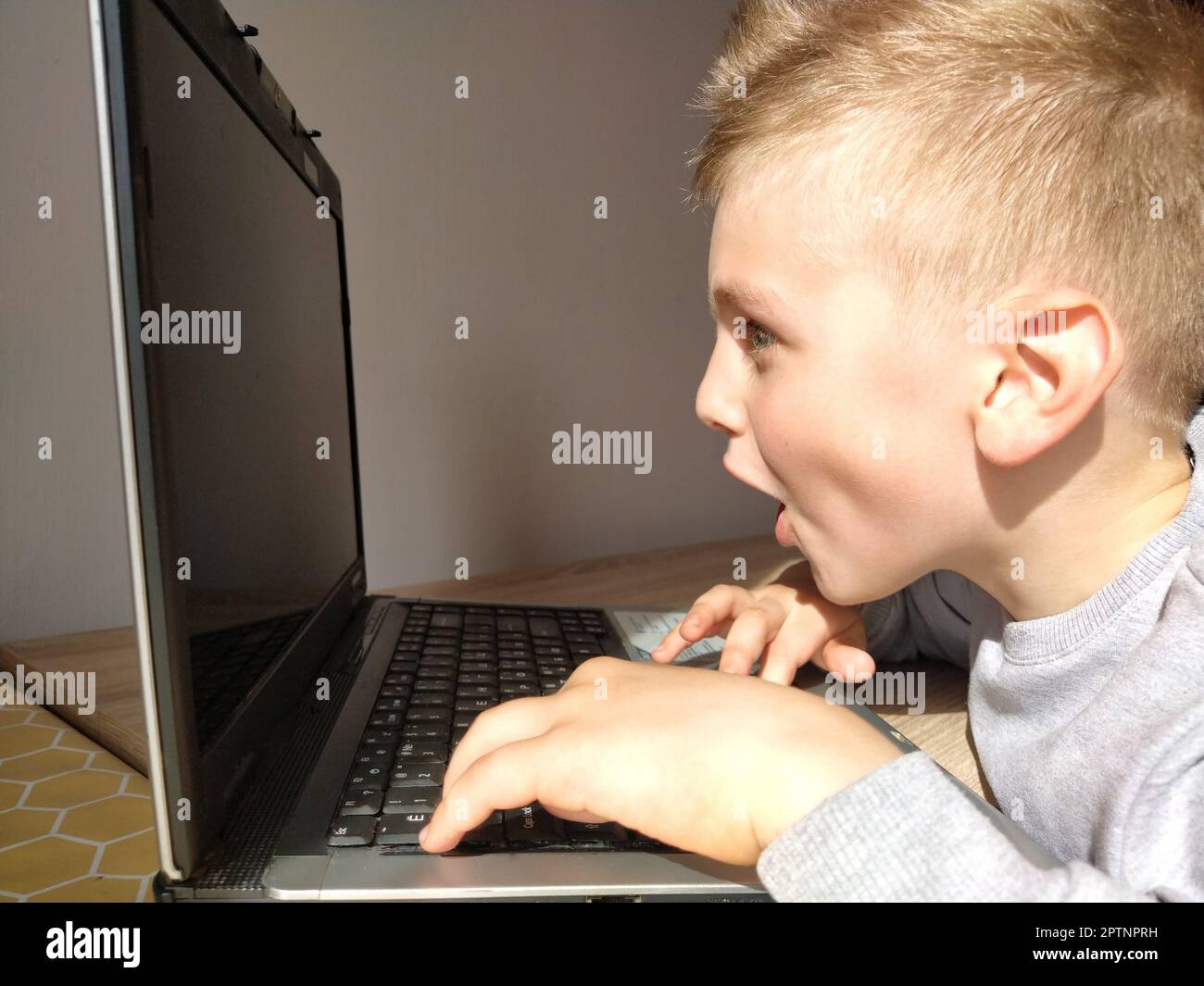 Cute kid with surprised expression in front of the laptop. The boy saw ...