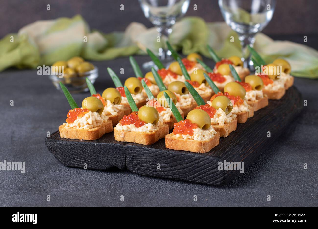 Canapes with red caviar and olives on croutons of white bread on dark ...