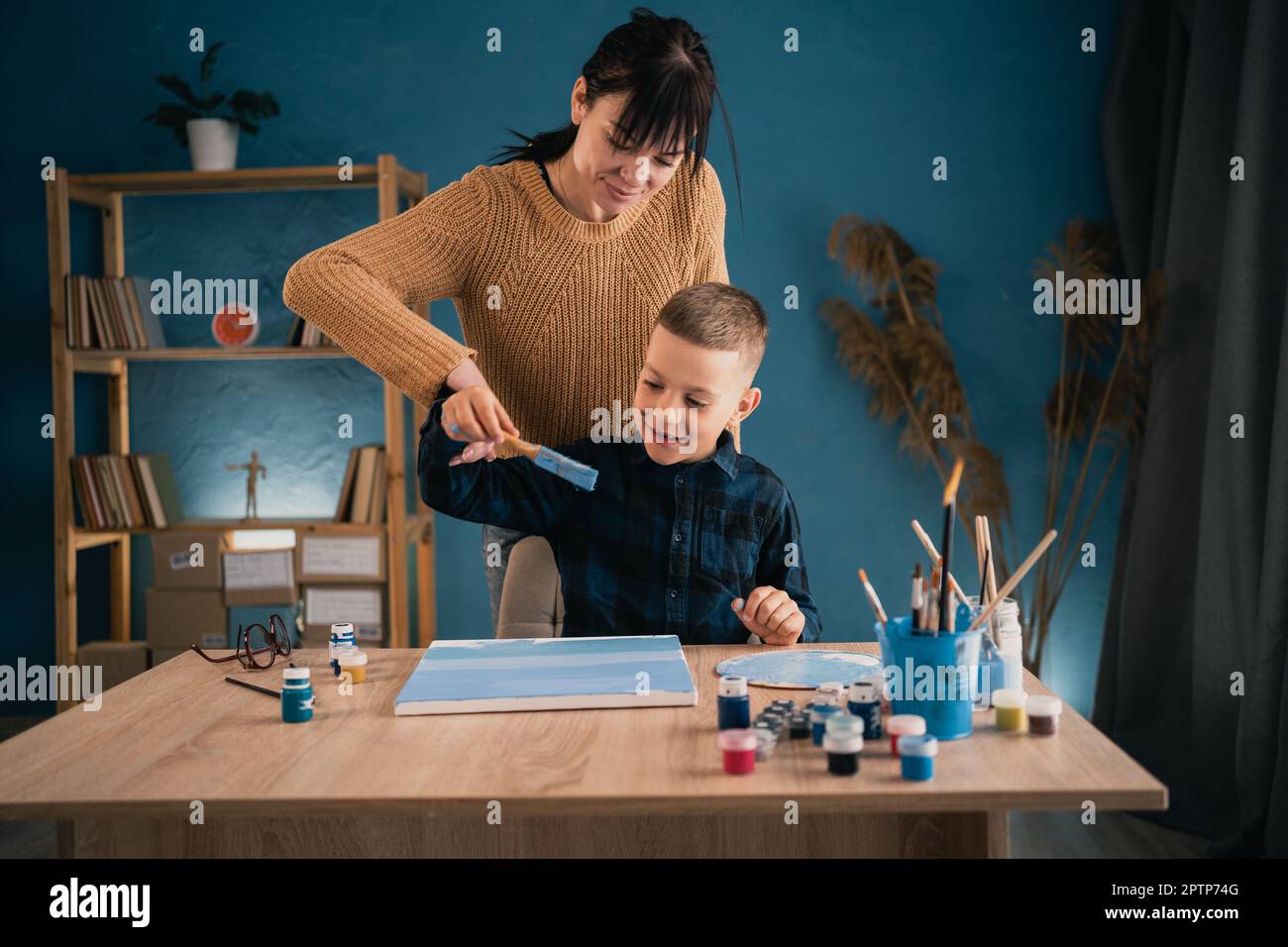 Art teacher gives a private lesson to a boy schoolboy at home. stands next to him and helps him ...