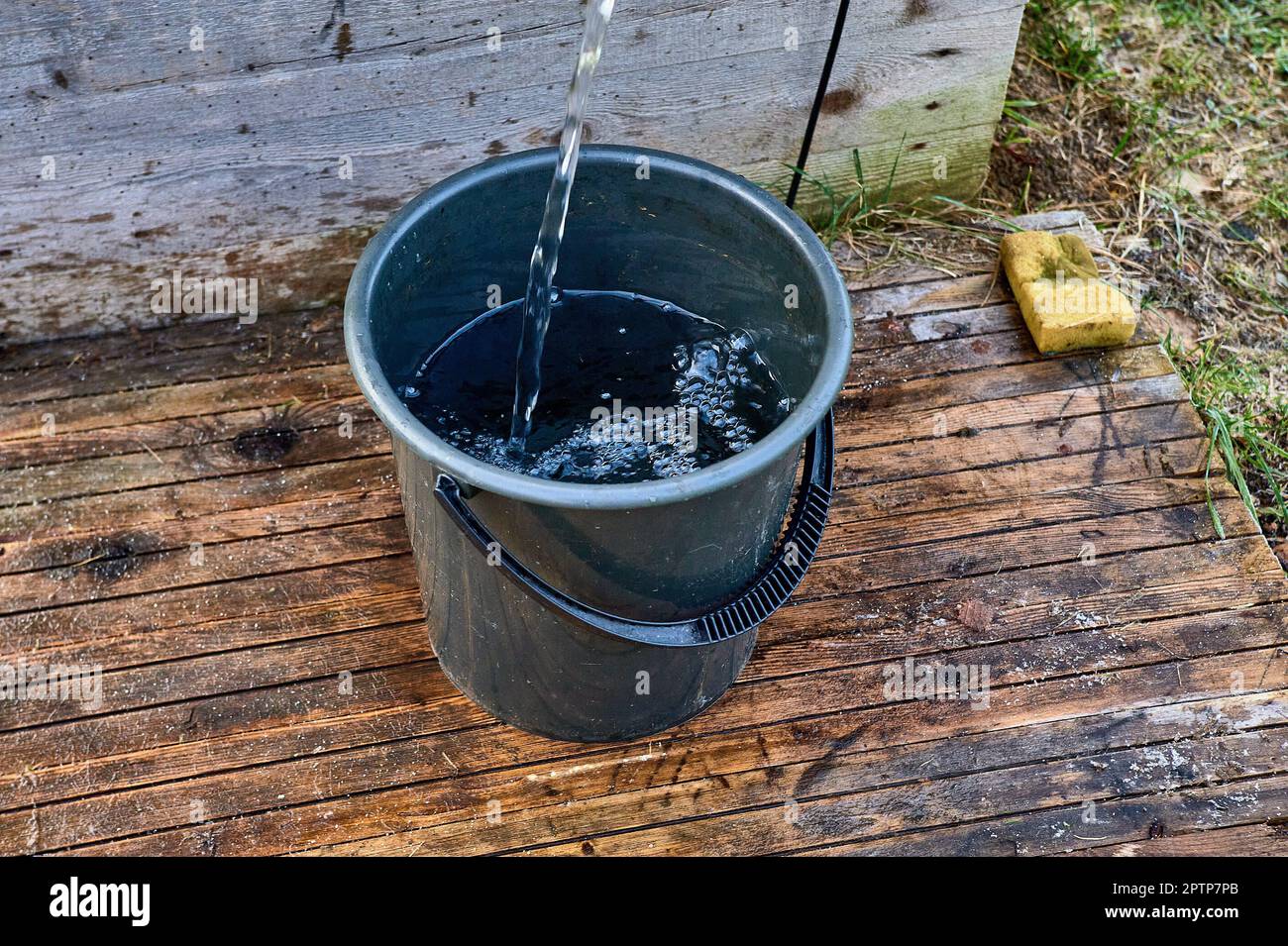 a black plastic bucket is filled with water from the pump. High quality ...