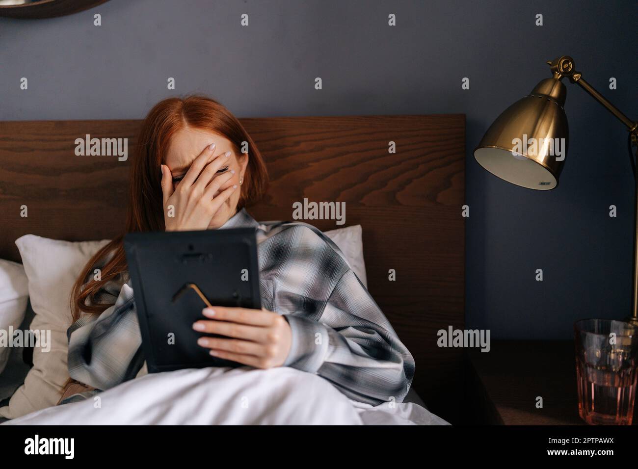 Portrait of grief-stricken young woman lying on bed covering face with ...