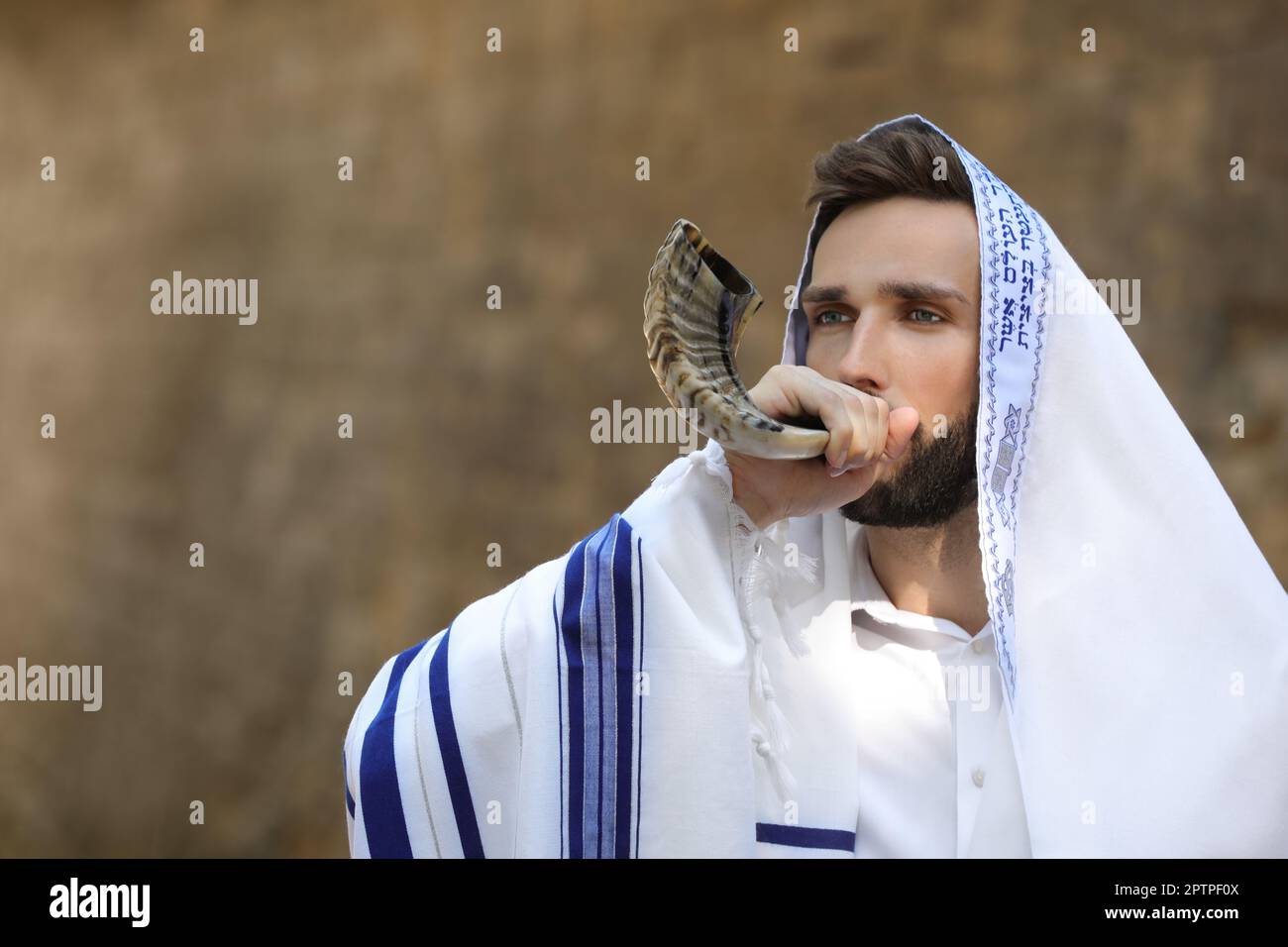 Jewish man blowing shofar on Rosh Hashanah outdoors. Wearing tallit ...