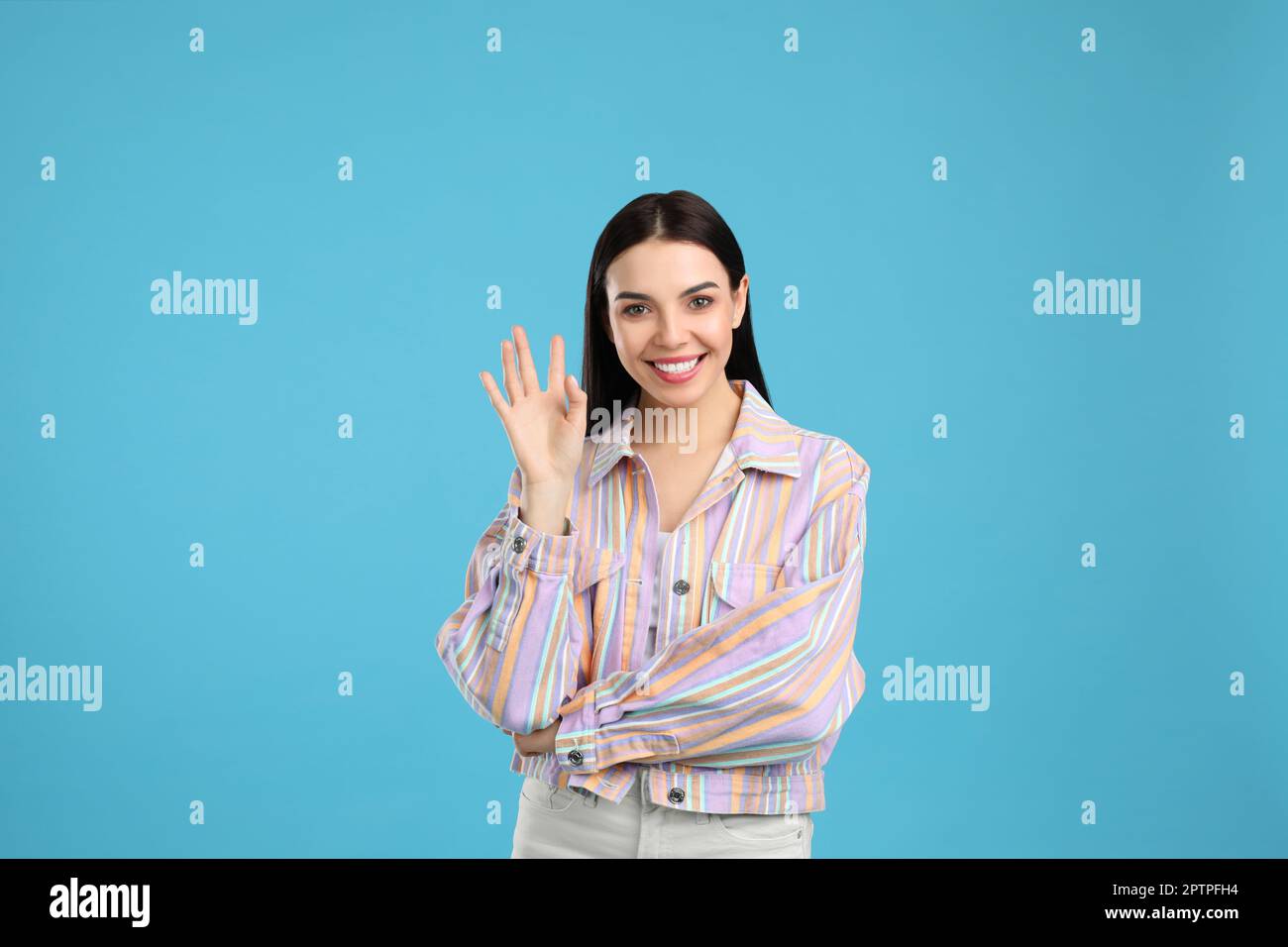 Attractive young woman showing hello gesture on light blue background ...