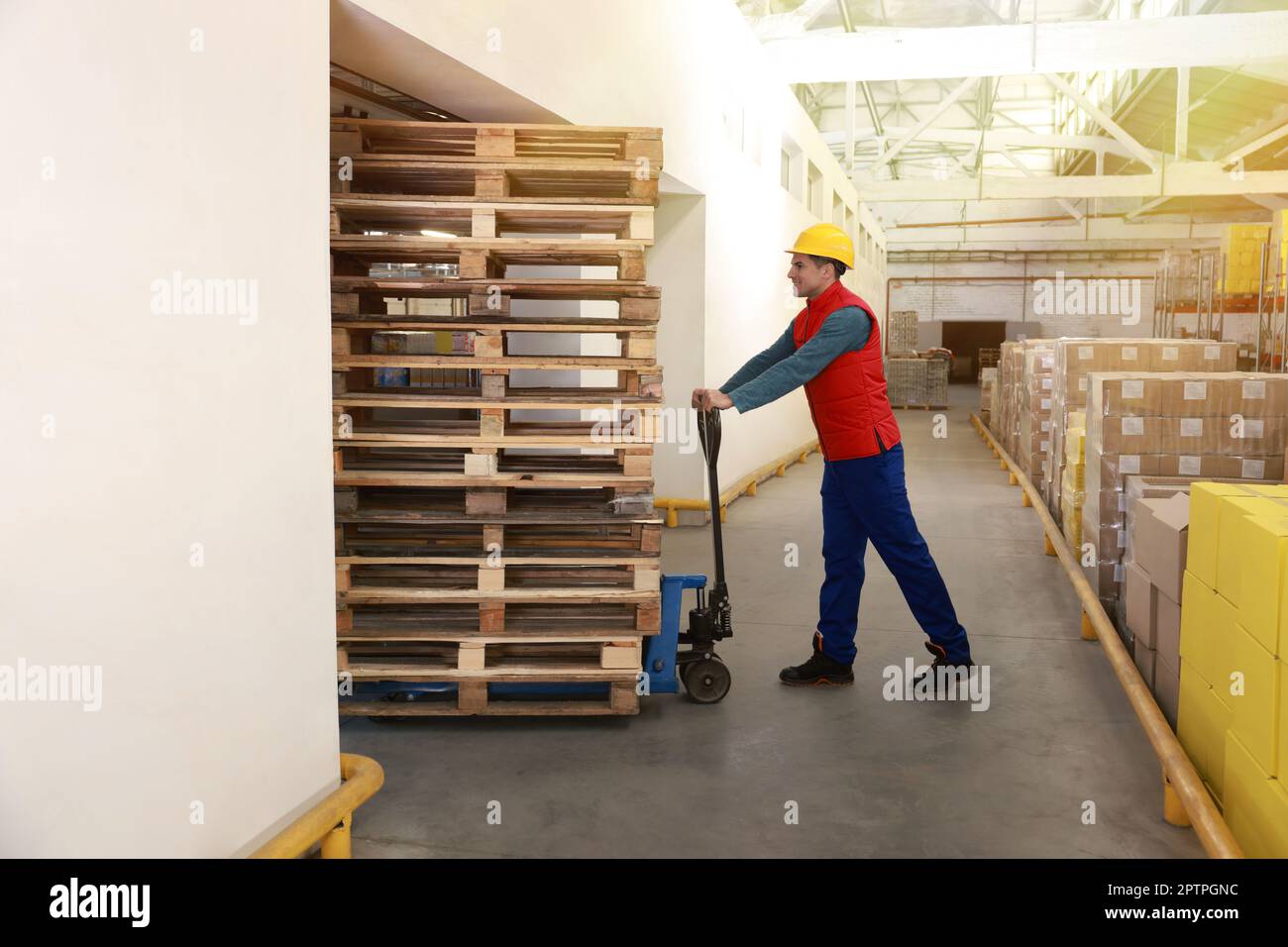 Worker moving wooden pallets with manual forklift in warehouse Stock ...