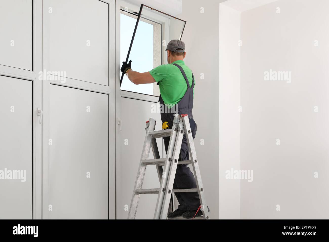 Worker on folding ladder installing window indoors Stock Photo - Alamy