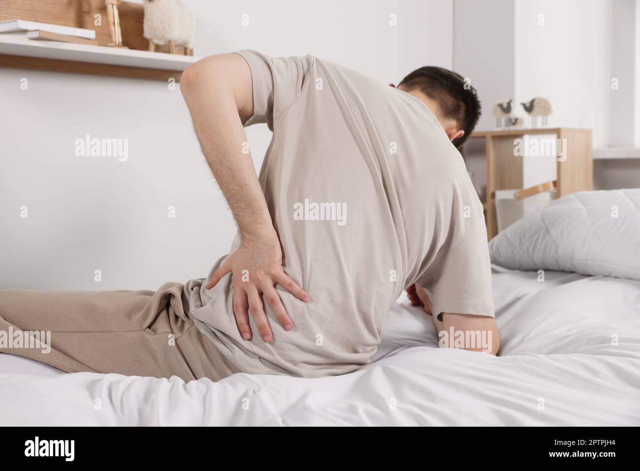 Man suffering from back pain while sitting on bed in room. Symptom of ...