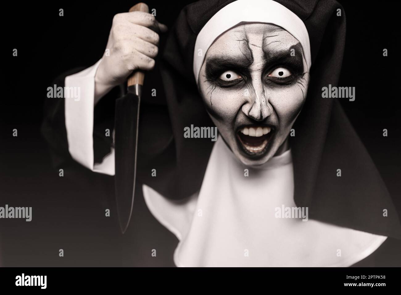 Scary devilish nun with knife on black background. Halloween party look ...