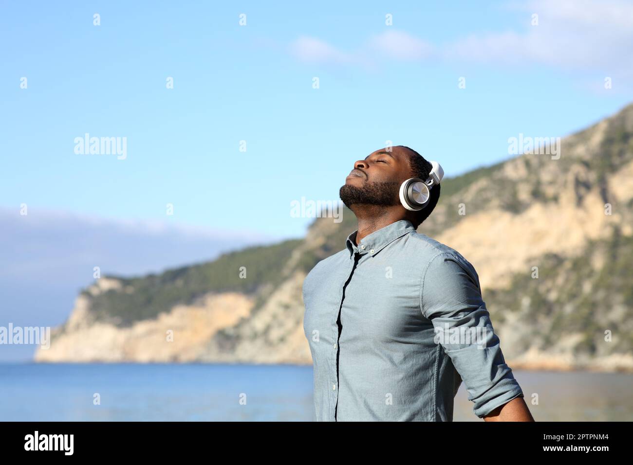 Relaxed black man meditating with wireless headphones listening a guide ...