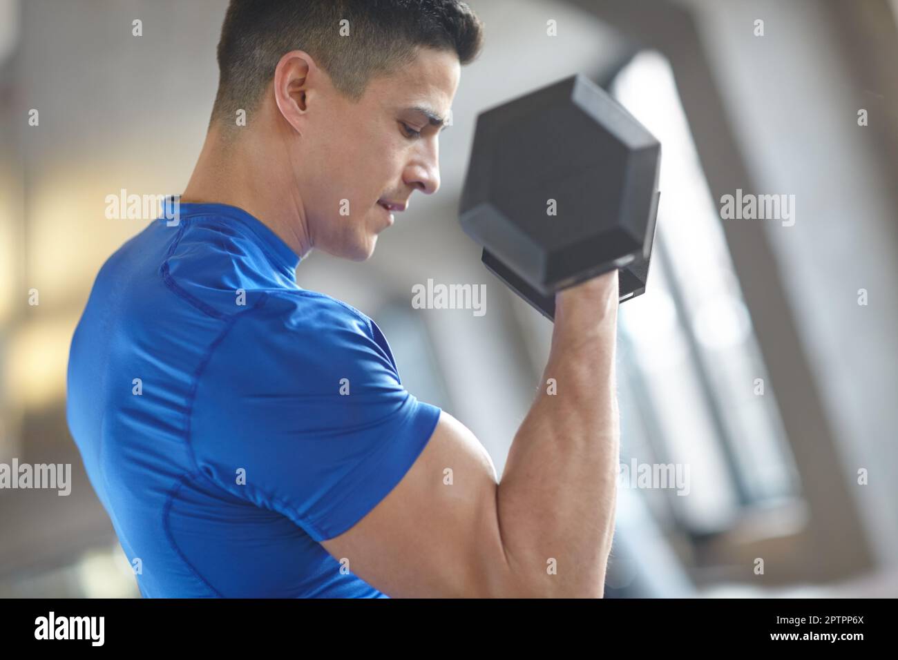 Concentrated power of will. a handsome young man lifting a dumbell in a ...