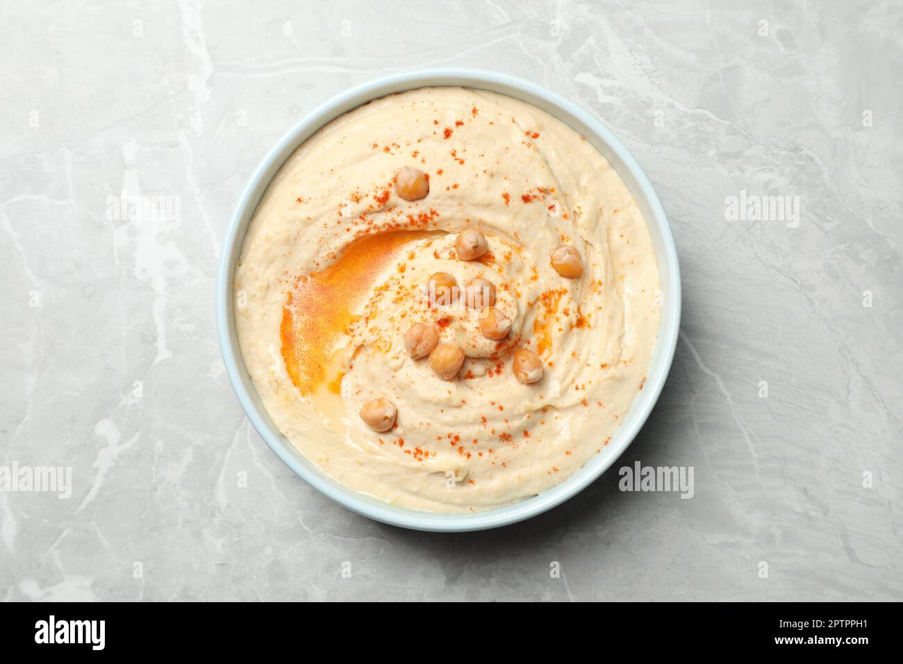 Tasty hummus with garnish in bowl on light grey marble table, top view ...